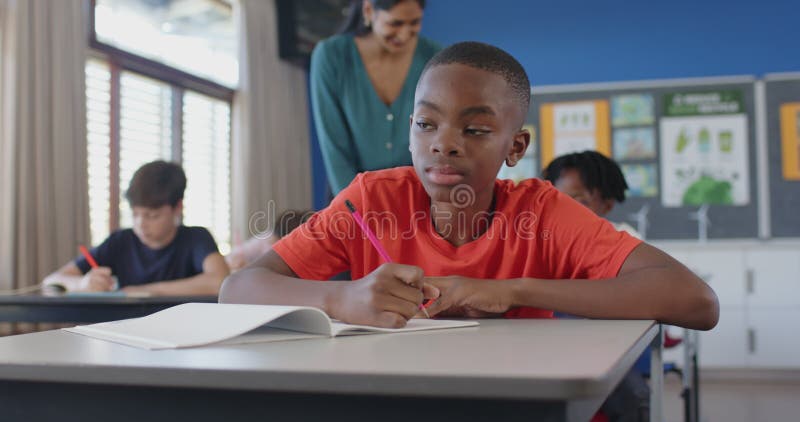 Smiling Boy in School Classroom Writing in Notebook with Classmates and ...