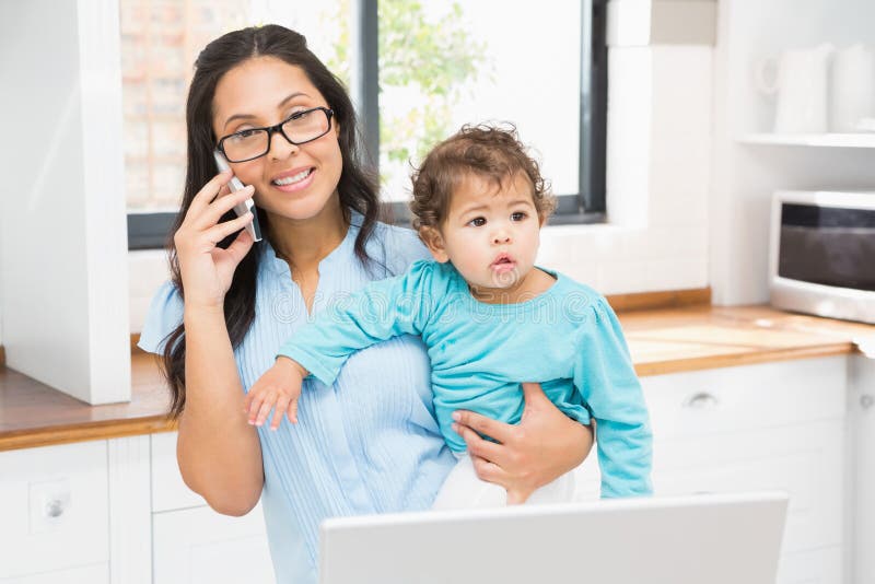 Smiling Brunette Holding Her Baby and Using Laptop on Phone Call Stock ...