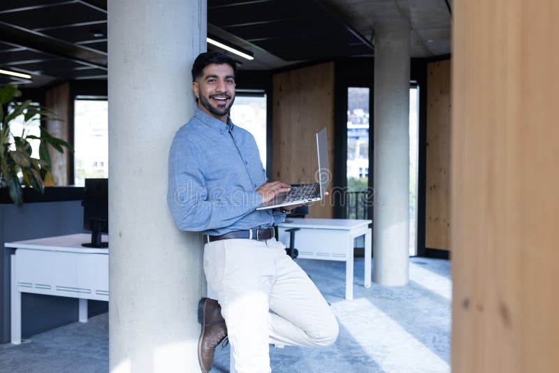 Smiling Businessman Leaning on Pillar Using Laptop in Modern Office ...