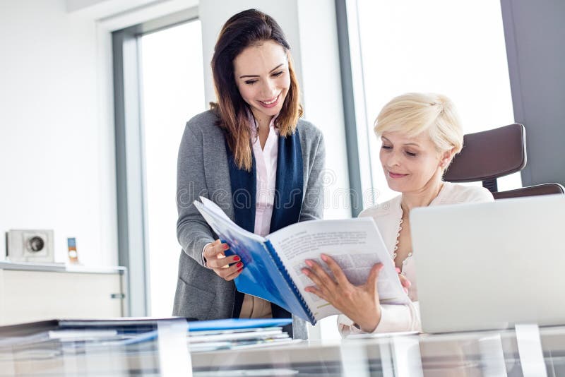 Smiling Businesswomen Reading Book at Desk in Office Stock Photo ...