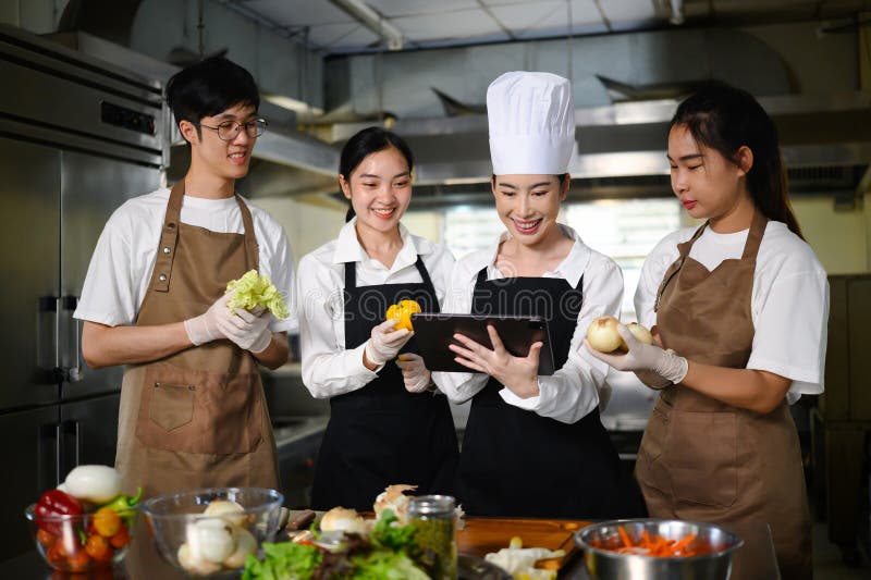Smiling Chef Teacher Using a Tablet To Explain a Recipe To Students in a Professional Kitchen ...