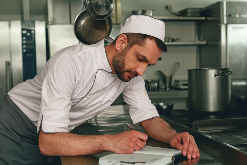 Smiling Chef in Uniform Making Notes in Notebook Standing on Kitchen ...