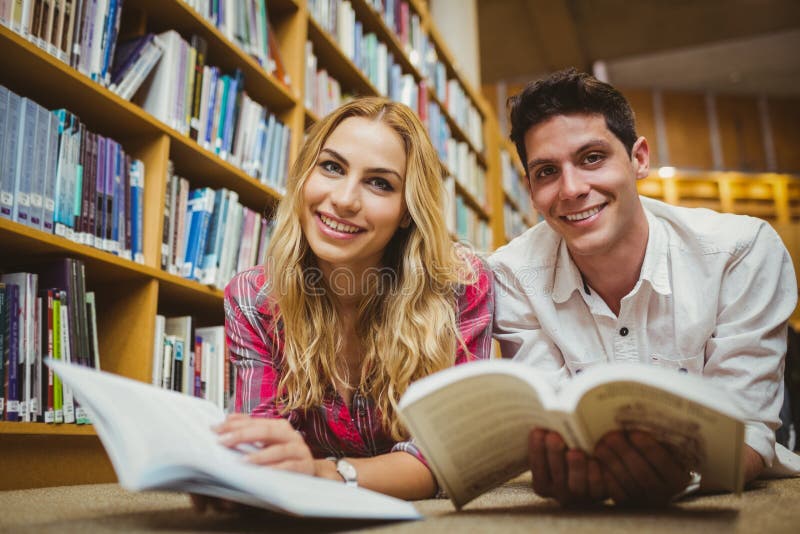 Smiling Classmates Reading Book while Leaning on Bookshelves Stock ...