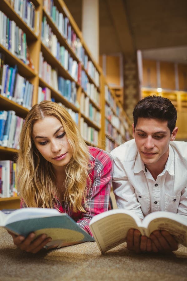 Smiling Classmates Reading Book while Leaning on Bookshelves Stock ...
