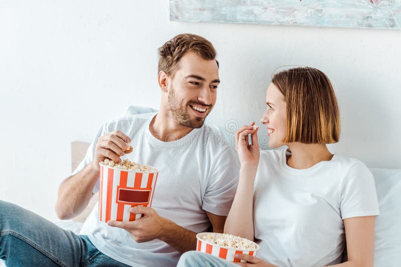 Smiling Couple Eating Popcorn in Bed and Looking at Each Other Stock ...