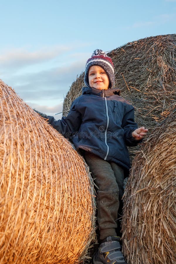 A Smiling Cute Boy with a Knitted Hat Stands on Hay Bales in the ...