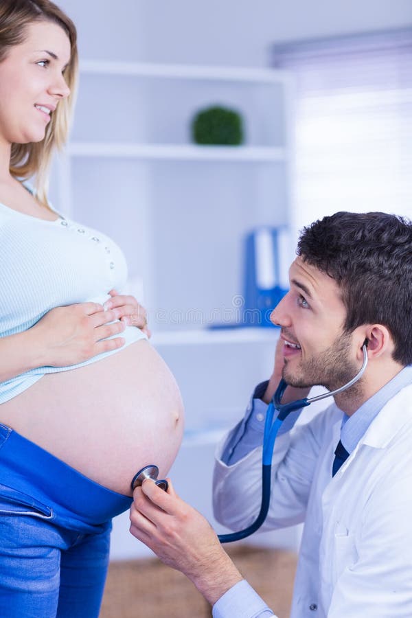 Smiling Doctor Examining Stomach Of Standing Pregnant Patient Stock