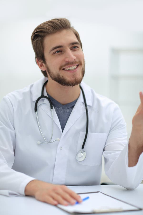 Smiling Doctor Sitting Behind a Desk Stock Photo - Image of indoors ...