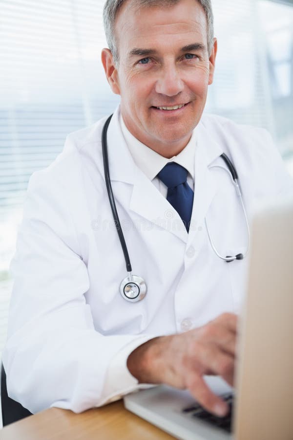 Smiling Experienced Doctor Typing on His Laptop Stock Photo - Image of ...