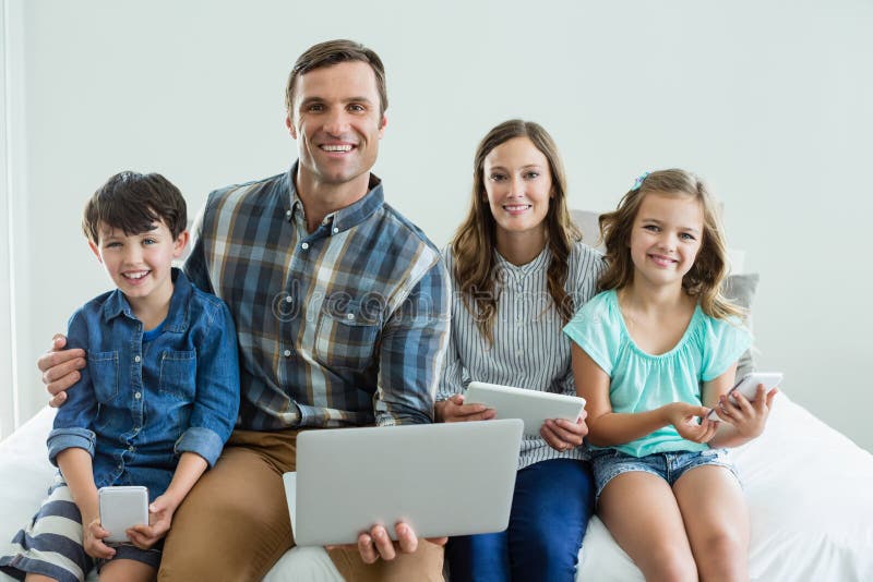 Smiling Family Using Laptop, Digital Tablet and Mobile Phone in Bedroom ...