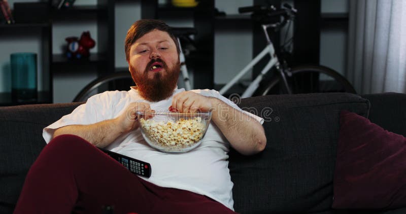 Smiling Fat Man with Beard Watches TV in the Room and Eats Pop-corn at ...