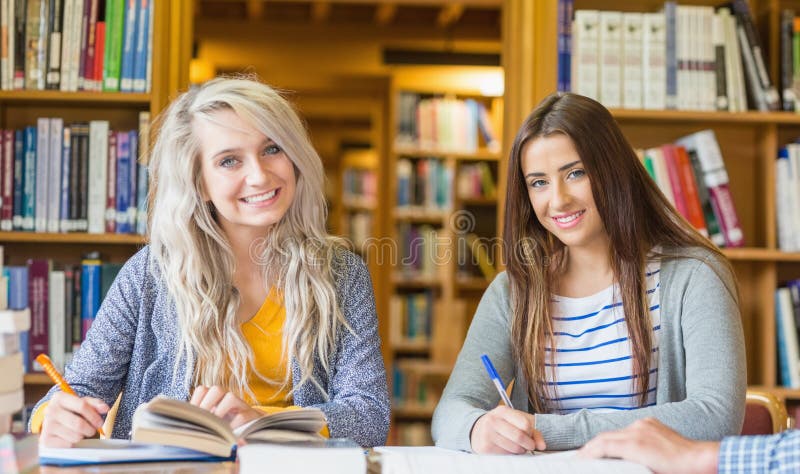 Smiling Female Students Writing Notes at Library Desk Stock Photo ...
