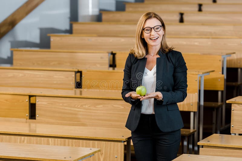 Smiling Female Teacher in Glasses and Formal Wear Holding Apple and ... Smiling Female Teacher in Glasses and Formal Wear Holding Apple and ...