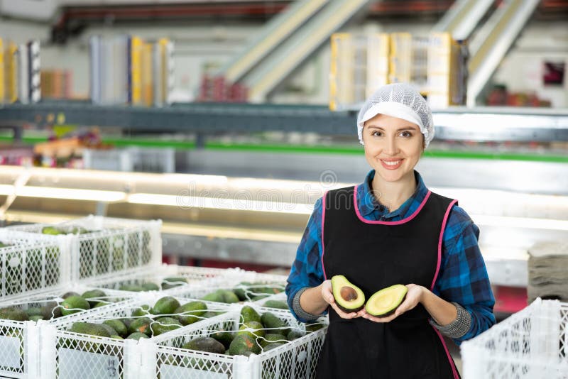 Smiling Female Worker in Fruit Sorting Warehouse Holding Sliced Avocado ...