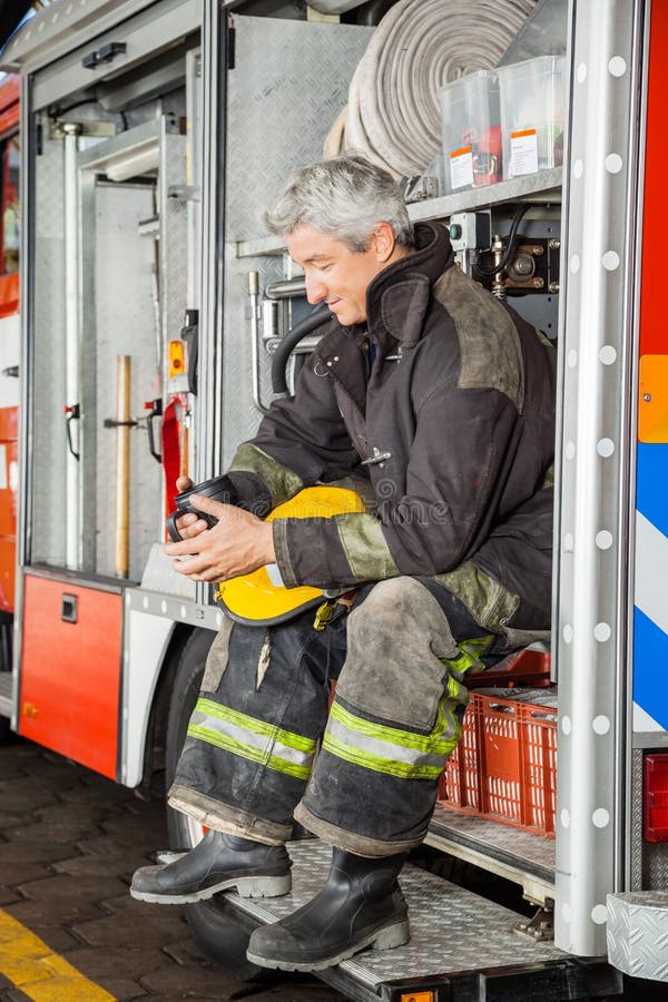 Smiling Fireman Looking at Coffee Mug while in Truck Stock Photo ...