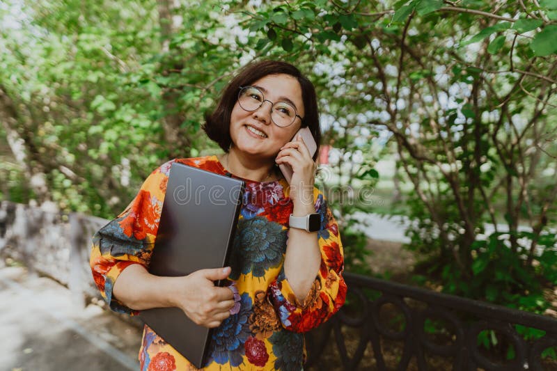 Smiling Freelancer Woman in a Laptop Using a Smartphone Outdoors in the ...