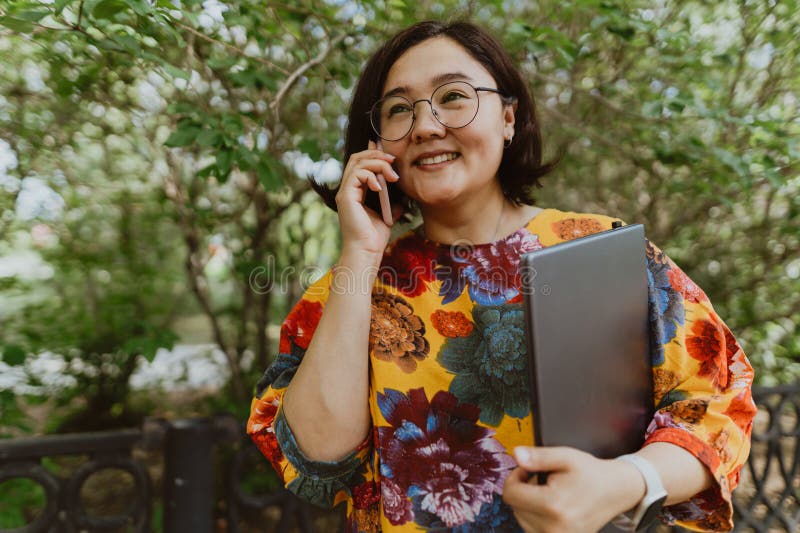 Smiling Freelancer Woman in a Laptop Using a Smartphone Outdoors in the ...