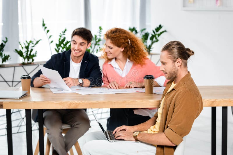 Smiling Friends Doing Paperwork and Using Laptop in Office Stock Photo ...