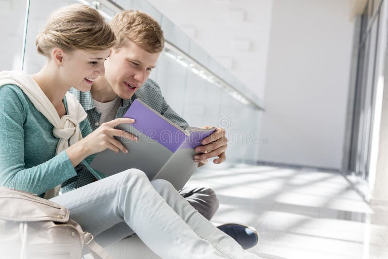 Smiling Friends Reading Book while Sitting on Corridor at University ...