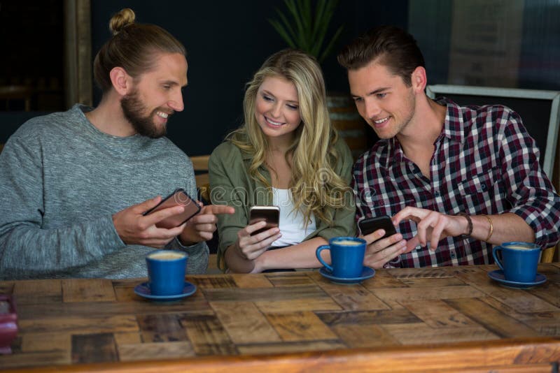Smiling Friends Using Smart Phones at Table in Cafeteria Stock Photo ...