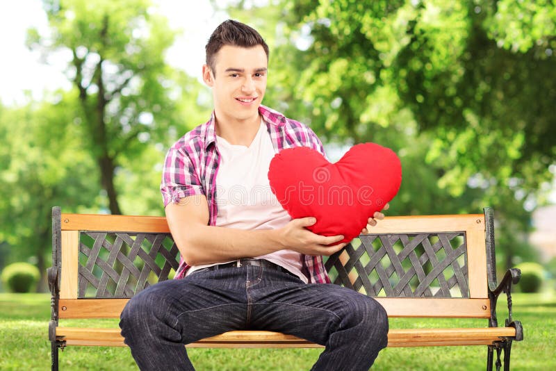 Smiling Guy Sitting on a Bench and Holding a Red Heart in Park Stock ...