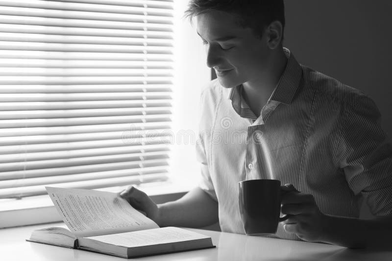 Smiling Guy Sitting at Table and Reading Book. Stock Photo - Image of ...