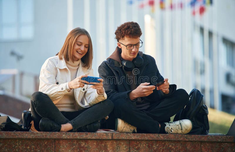 Smiling, Having Fun. Two Young Students are Sitting Outdoors Against ...