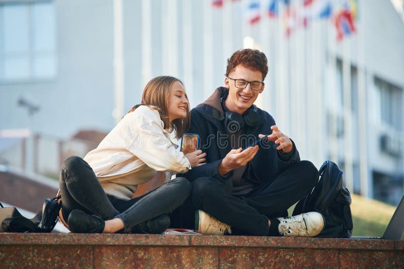 Smiling, Having Fun. Two Young Students are Sitting Outdoors Against ...