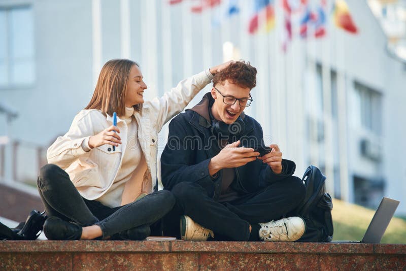 Smiling, Having Fun. Two Young Students are Sitting Outdoors Against ...