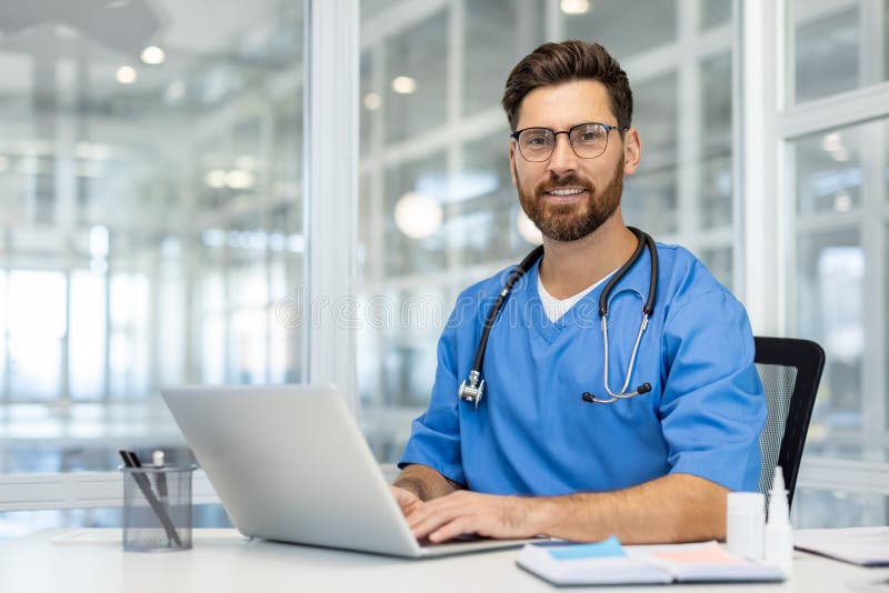 Smiling Healthcare Professional in Blue Scrubs Working on a Laptop in ...