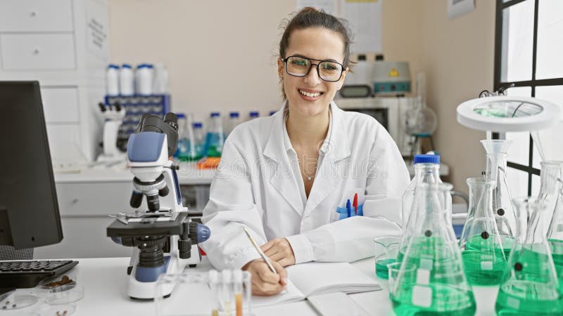 A Smiling Hispanic Woman Scientist Writing in a Notebook in a ...