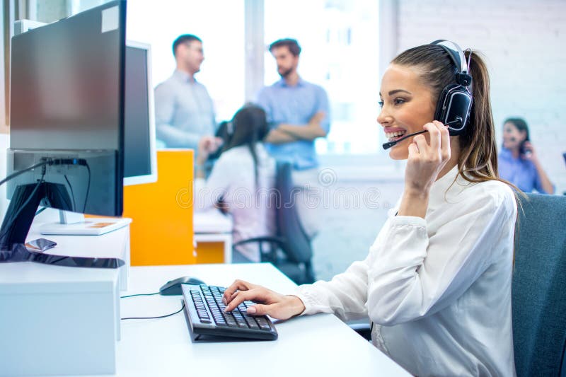 Smiling Hotline Operator Woman with Headset Using Computer in Office ...
