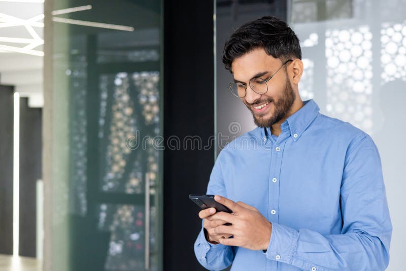 Smiling Indian Man Standing in Modern Office and Using Mobile Phone ...