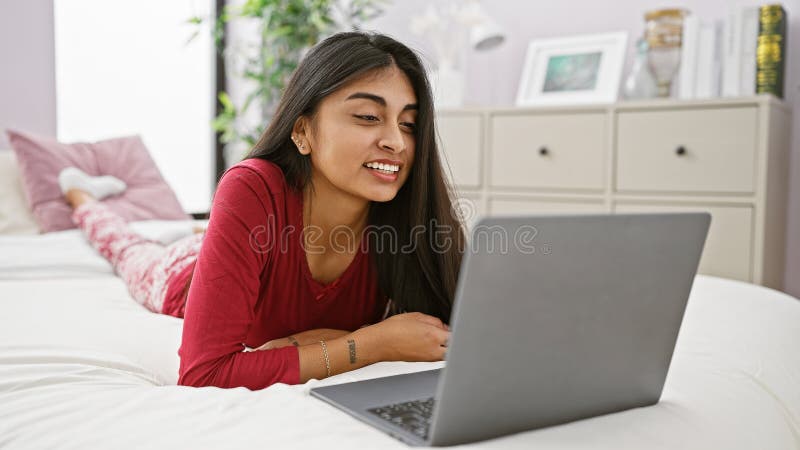 Smiling Indian Woman Lying on Bed Using Laptop in a Bright Bedroom ...