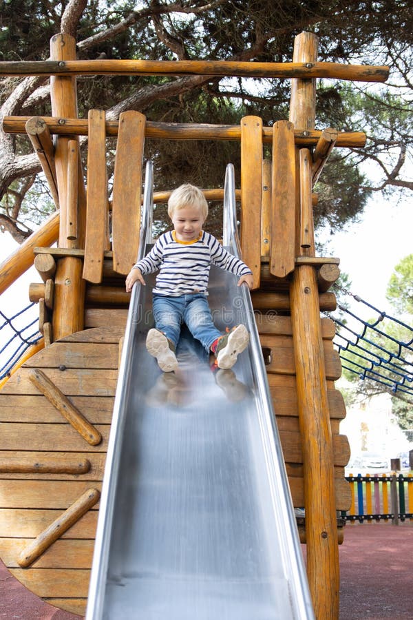 Smiling Little Blonde Boy Slide Down a Slide on the Playground Stock ...