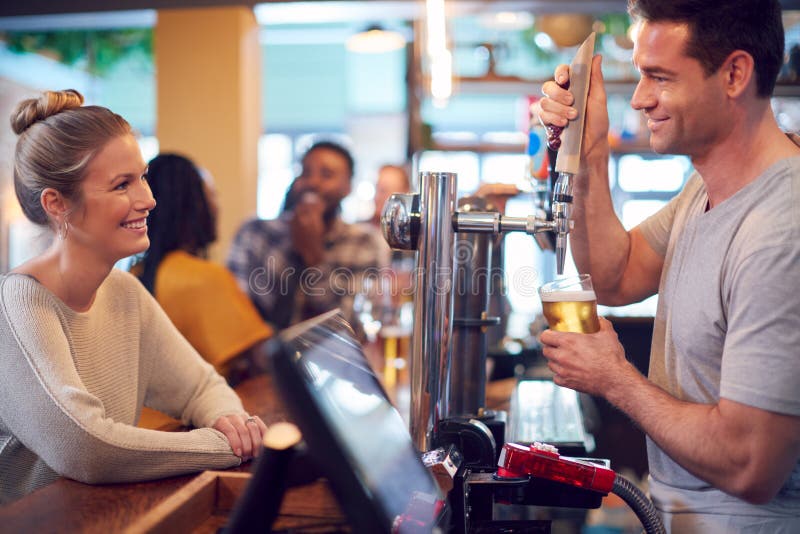 Smiling Male Bartender Behind Counter Serving Female Customer with Beer ...