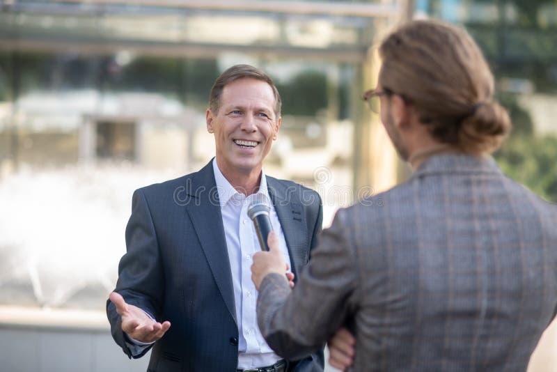 Smiling Male Speaking into Microphone, Answering Long-haired Journalist ...