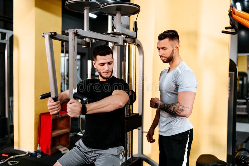 Smiling Man Learning at the Gym, Doing Chest Exercises with Assistance ...