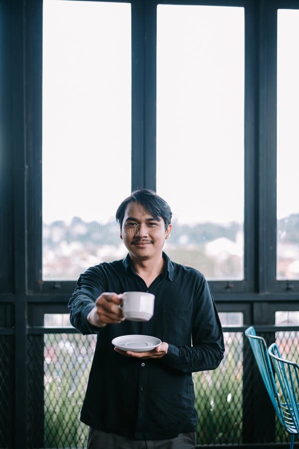 Smiling Man Offering Coffee Indoors with Architectural Backdrop Stock ...
