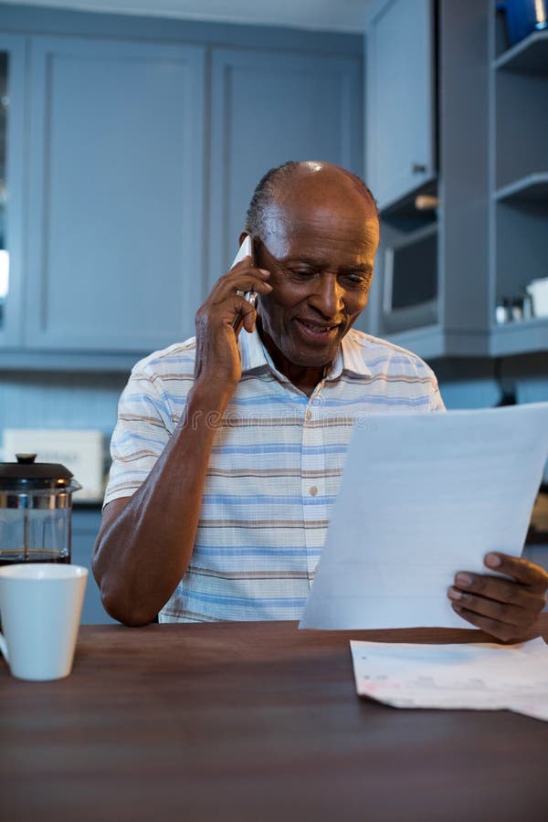 Smiling Man Reading Document while Using Phone at Home Stock Image ...