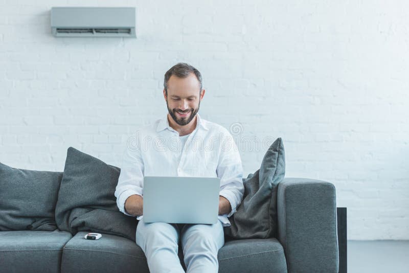 Smiling Man Using Laptop and Sitting on Sofa with Air Conditioner Stock ...