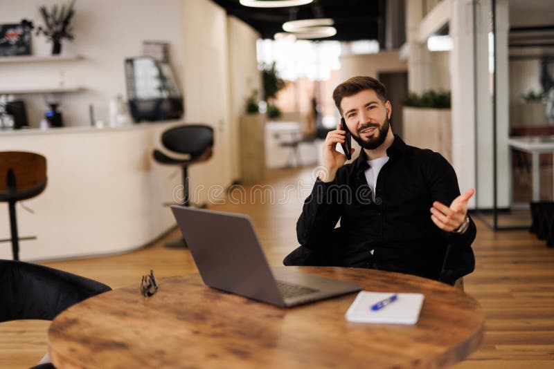 Smiling Man Writing Notes while Making Phone Call and Using Laptop at ...