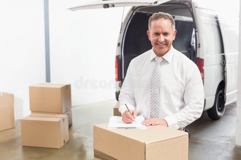 Man Leaning on Cardboard Box Writing on Clipboard Inside Warehouse by ...
