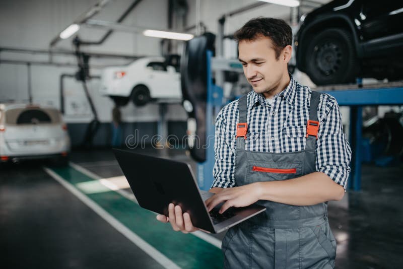 Smiling Man Mechanic Using a Laptop Computer To Check a Car Engine ...