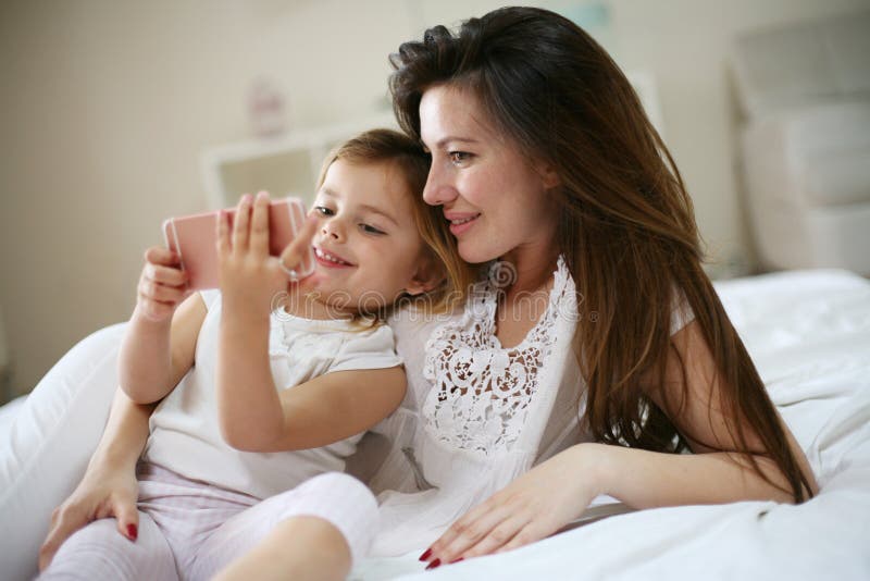 Smiling Mother with Daughter Using Smart Phone on Bed. Stock Photo ...