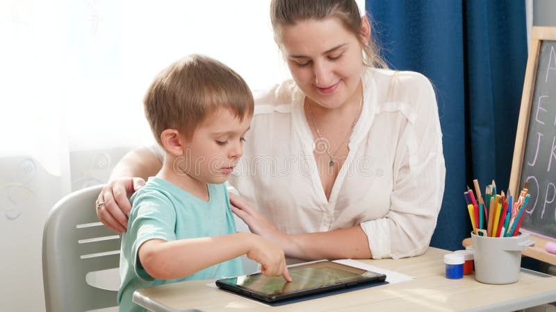 Smiling Mother Hugging and Caressing Her Smart Child Studying on Tablet ...