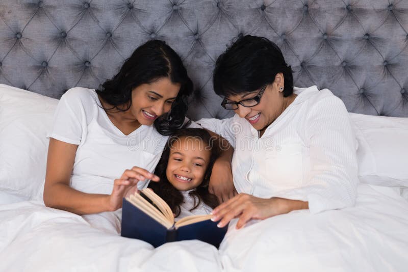 Smiling Multi-generation Family Reading Book while Resting on Bed Stock ...