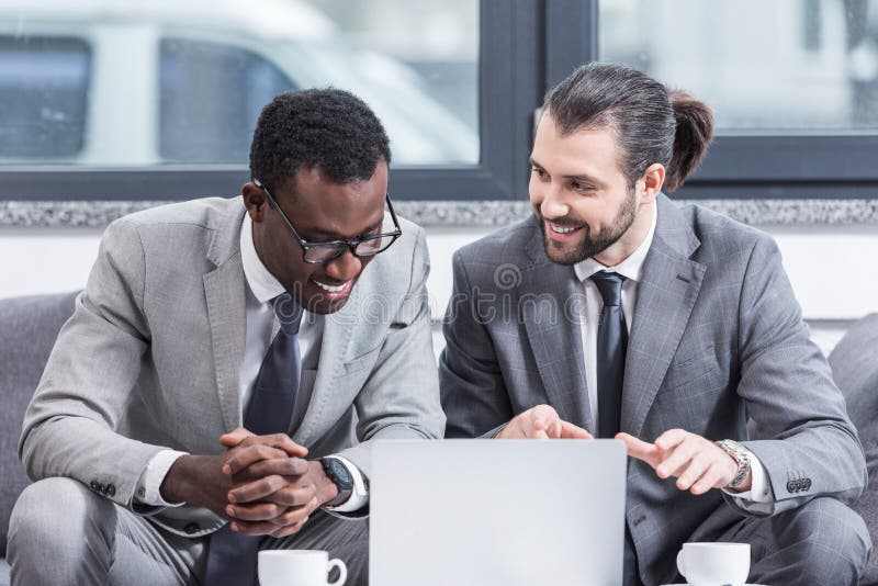Smiling Multicultural Businessmen in Suits Sitting at Table with Laptop ...
