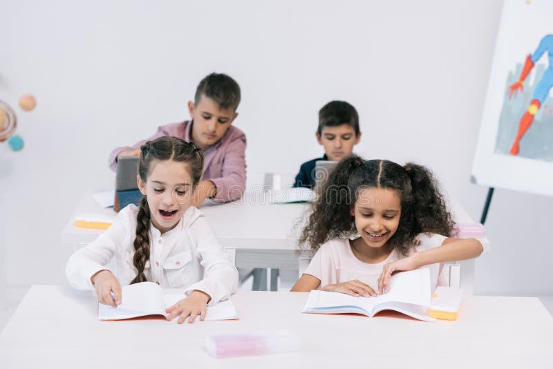 Smiling Multiethnic Pupils Studying with Textbooks in Classroom Stock ...