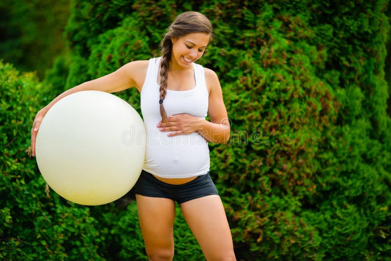 Smiling Pregnant Woman Touching Belly While Holding Exercise Bal Stock